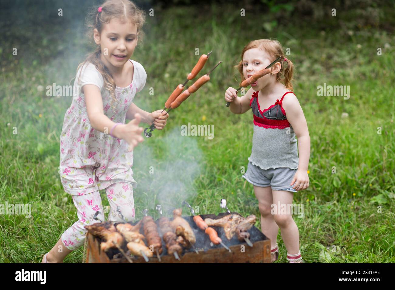 Two little girl making barbecue on the grill on nature, one girl eating ...