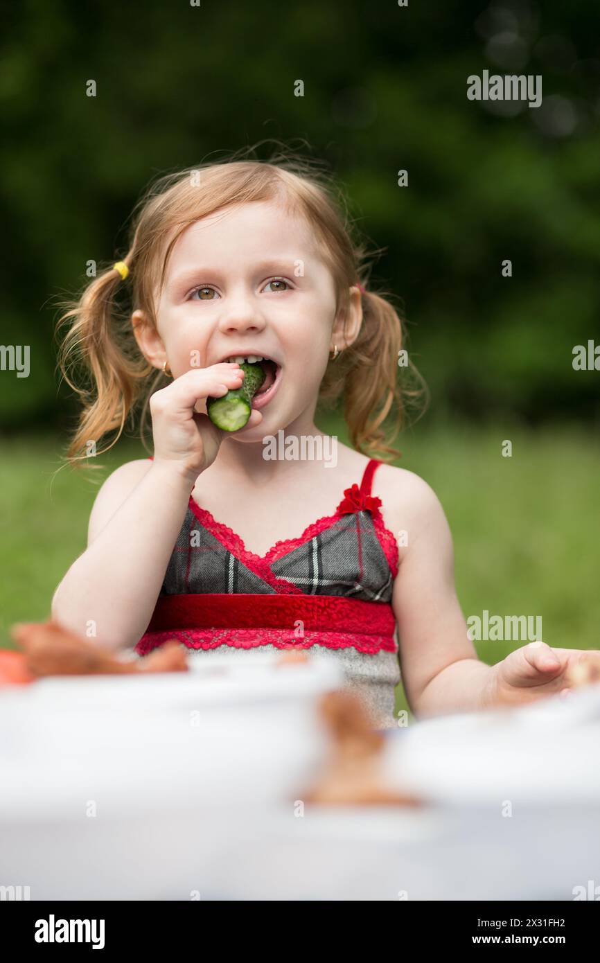 Little girl eats a cucumber in nature Stock Photo - Alamy