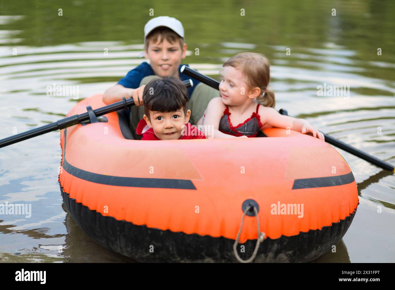 Three children float on a rubber boat with oars, focus on little boy ...
