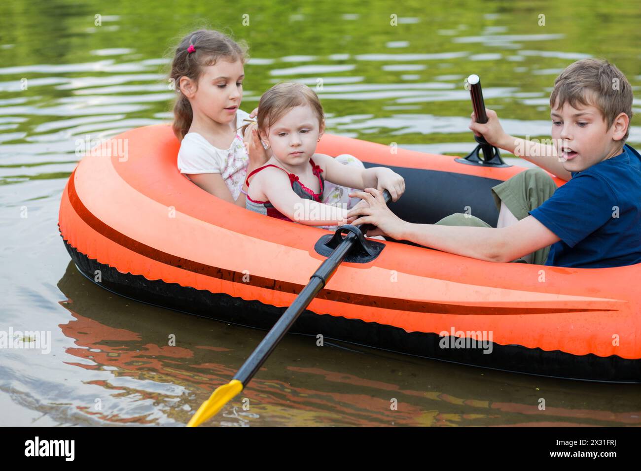 Three children floating in a rubber boat on the pond Stock Photo - Alamy