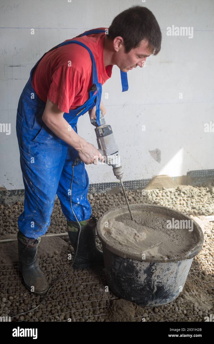 Worker prepare the mixture to fill the floor, focus on a bucket with ...