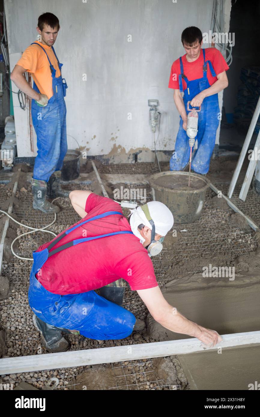 Three workers in construction room prepare the mixture and pouringl the ...