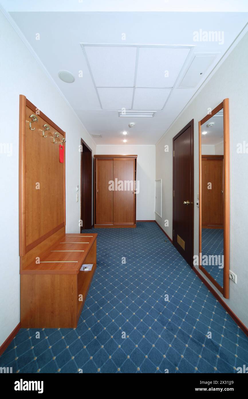Simple antechamber with wooden closet, mirror and blue carpet flooring ...
