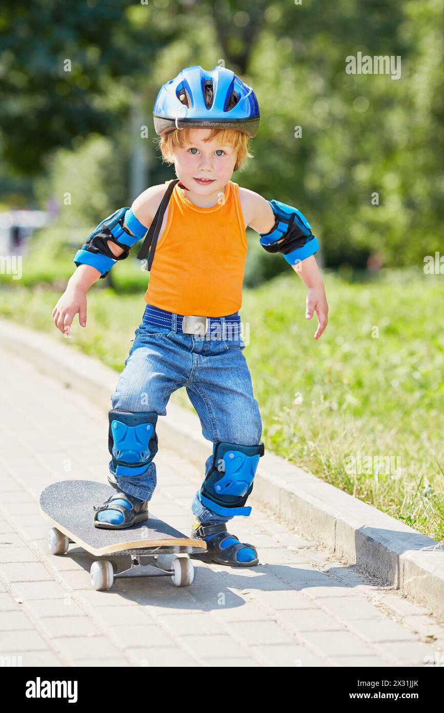 Little skateboarder stands on park alley with one his foot on ...