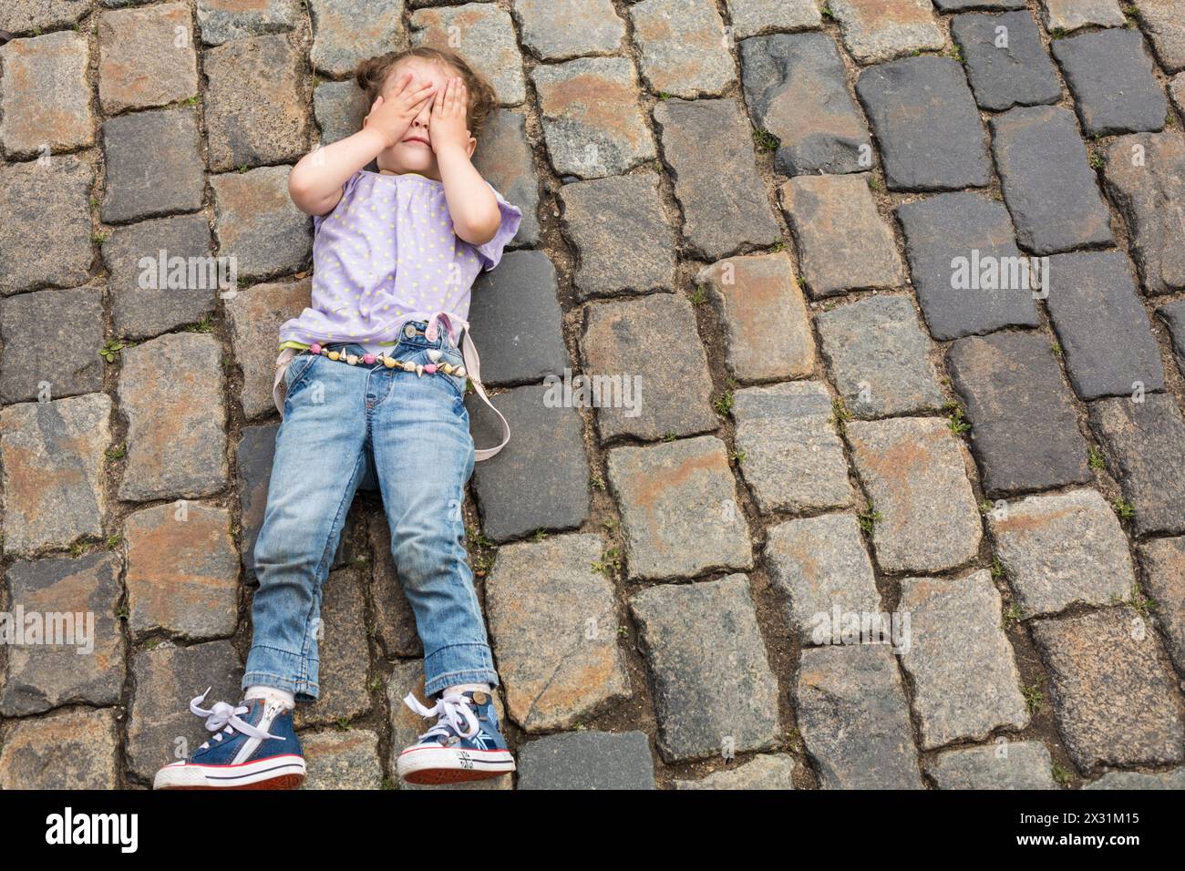 Little girl lying on the pavement covering eyes with hands Stock Photo ...