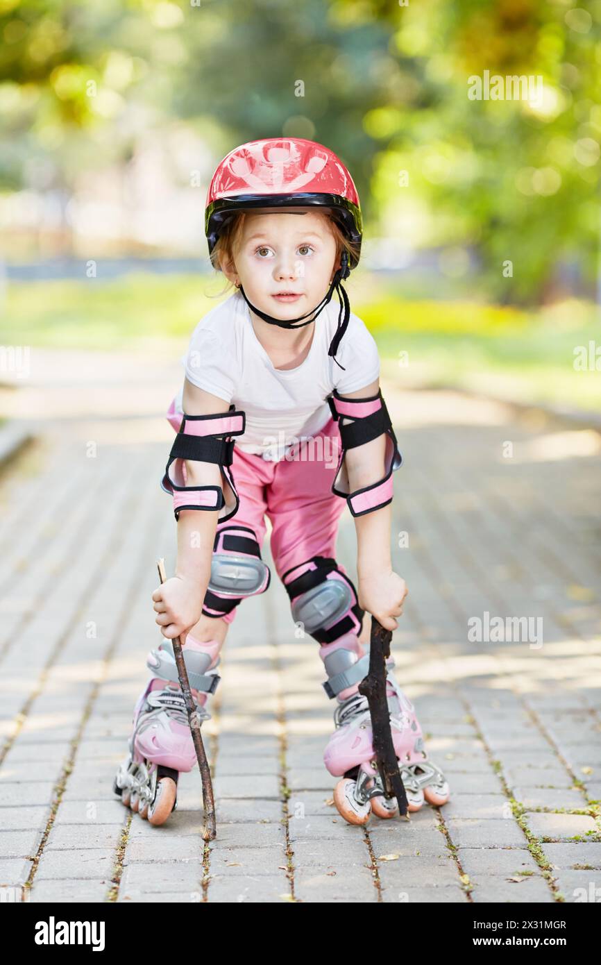 Little girl in protective equipment and rollers stands on park walkway ...