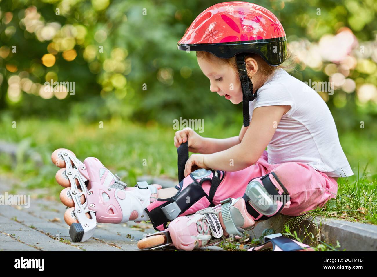 Little girl in protective equipment and rollers fastens knee-pad ...