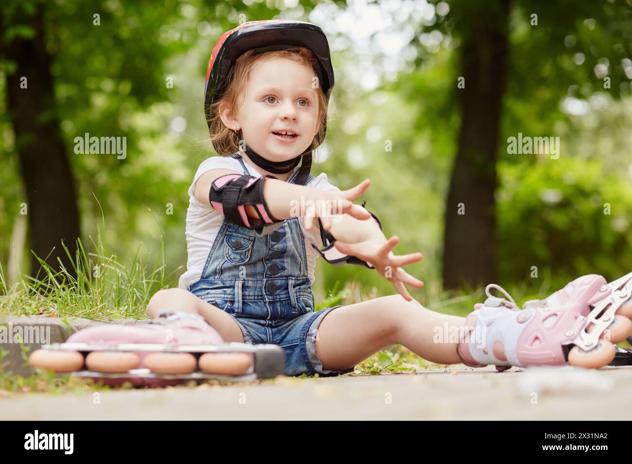 Little girl in protective equipment and rollers sits on ground on ...