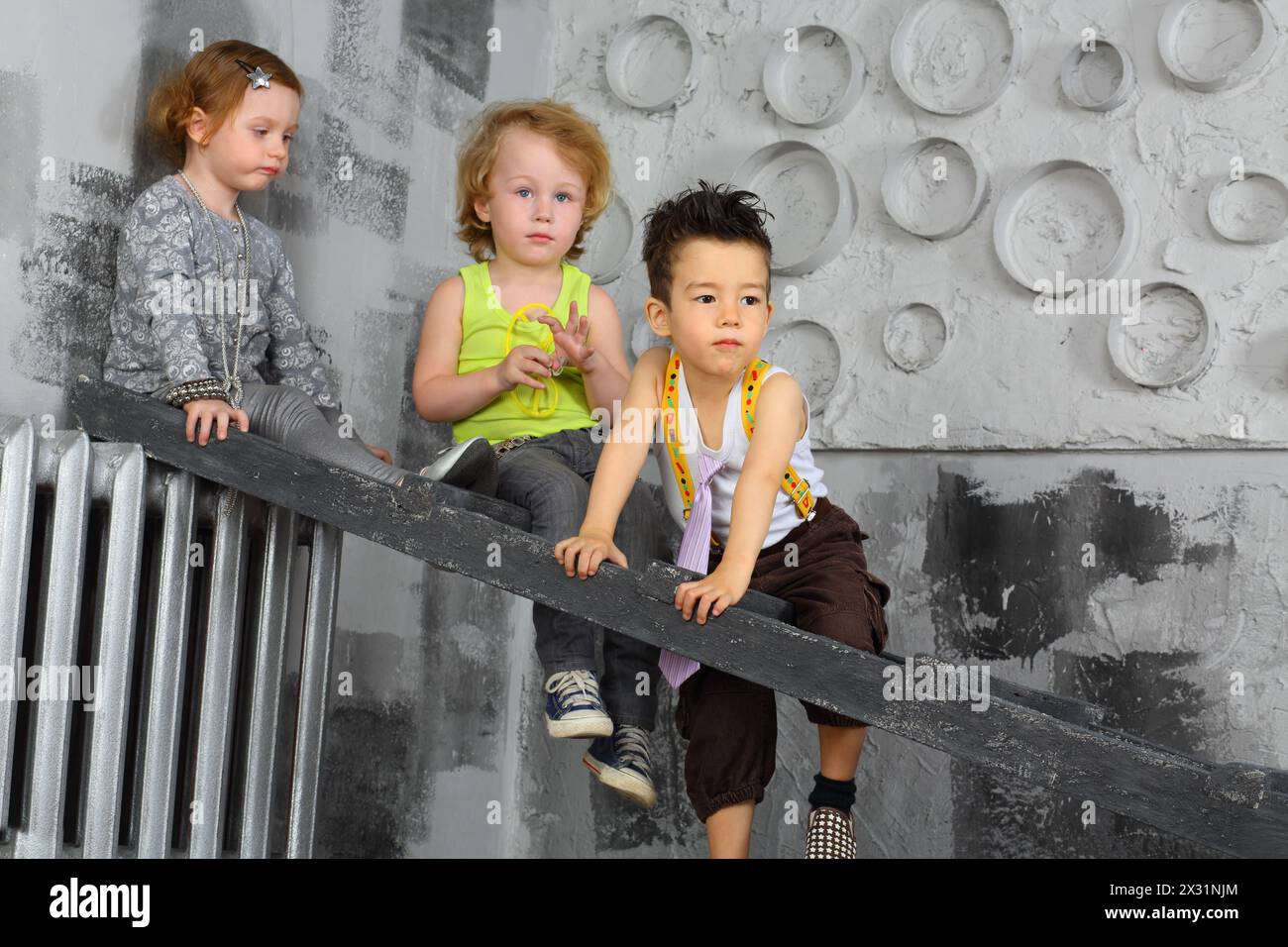 Three bored children sitting on the stairs near the gray wall Stock ...