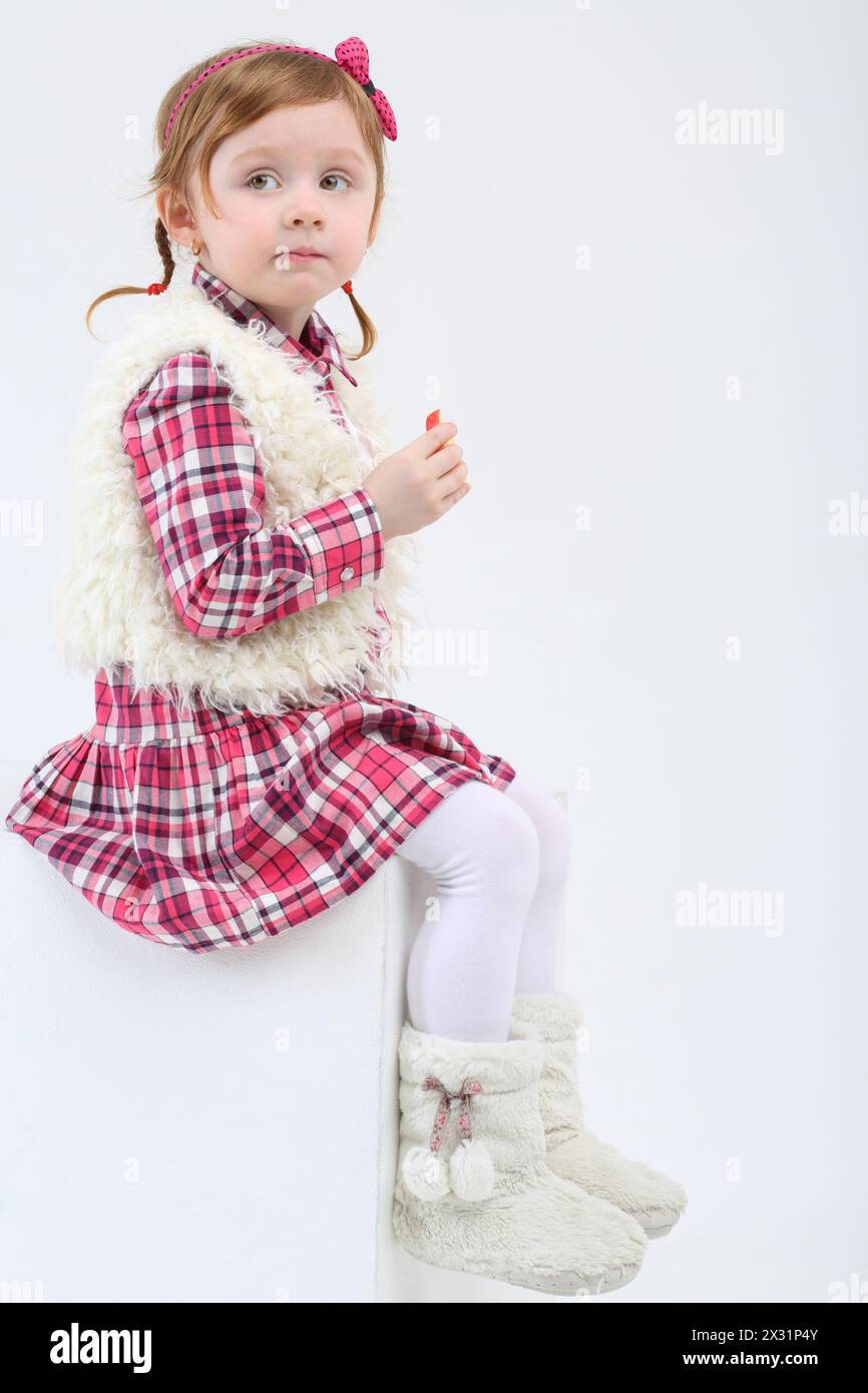 Little cute girl in fur boots sits on cube, eats piece of apple and ...