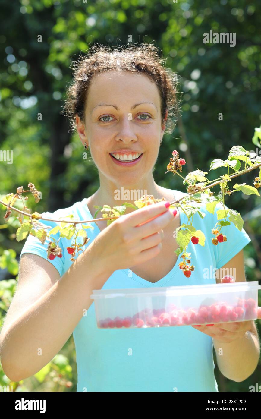 A smiling young woman gathering raspberries in the garden Stock Photo ...