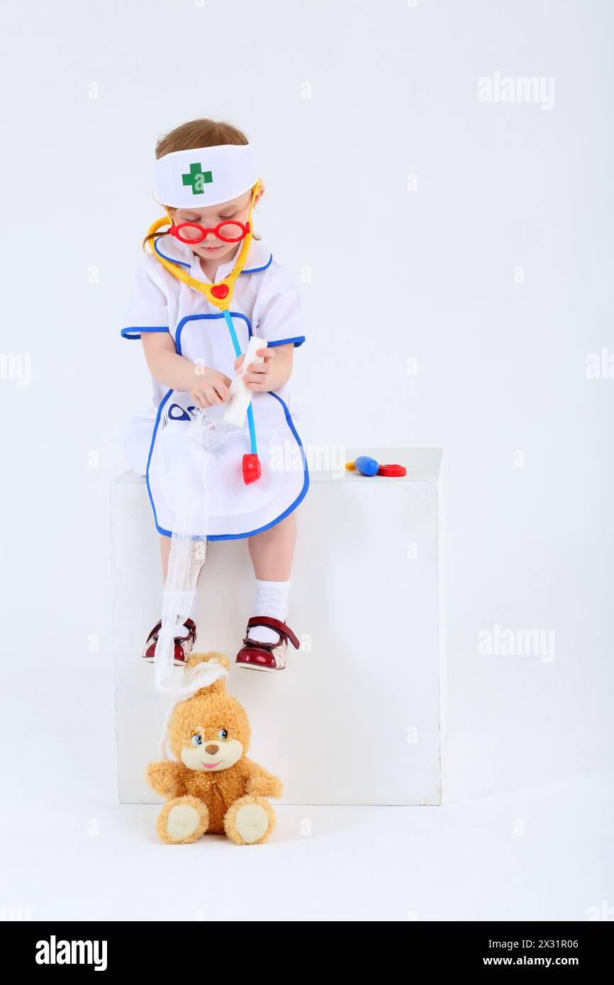 Little girl dressed as nurse bandages head to toy rabbit and sits on ...