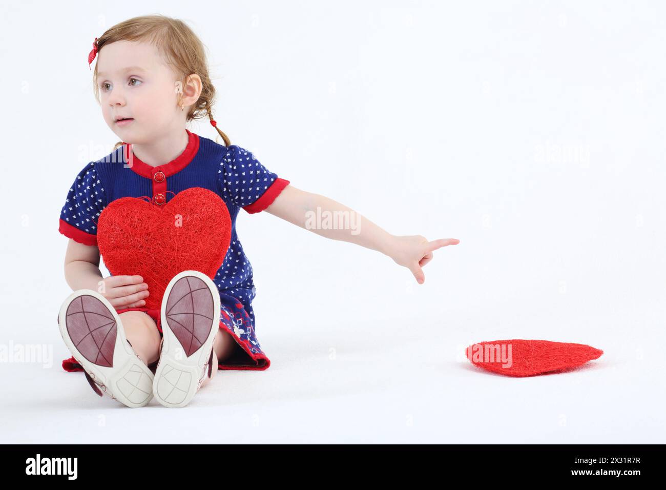 Little beautiful girl sits with red heart and reaches out to another ...
