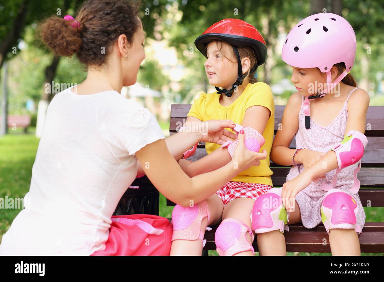 Young woman helping to put on elbow pads two girls in a park Stock ...