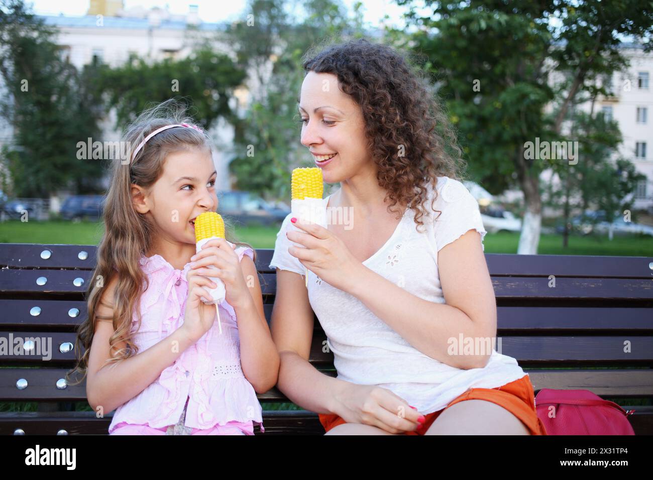 A mother and daughter sitting on the bench and eating boiled corn Stock ...