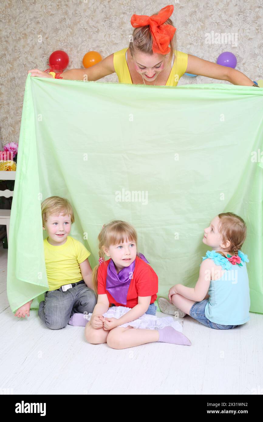 Three happy kids play with holiday host with cloth at funny children ...