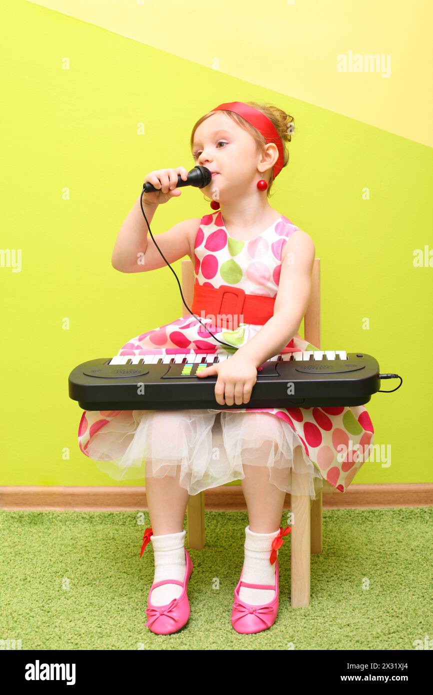 Girl in a bright dress sitting on a chair and sings, on her lap toy ...