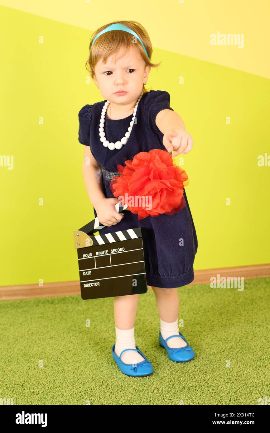 Little girl holding a clapstick in her hand and points a finger forward ...