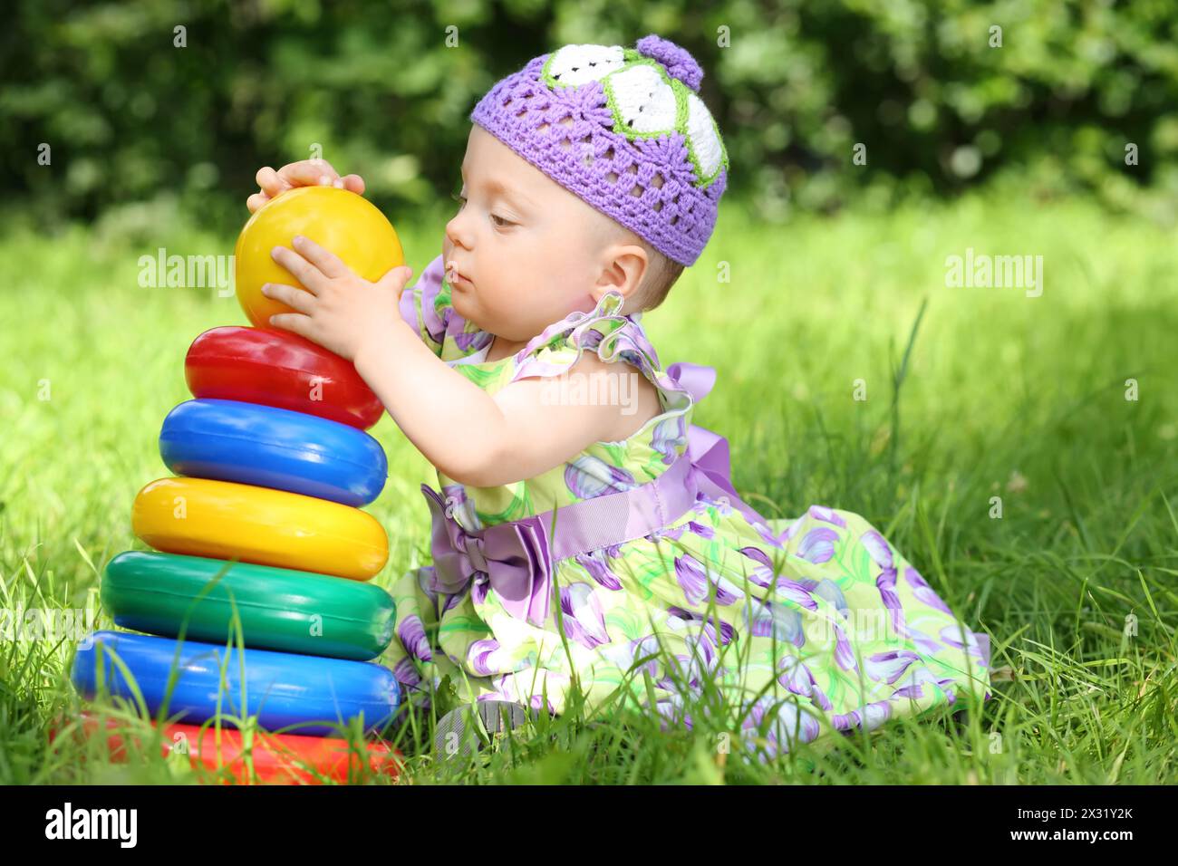 Little girl playing with colorful pyramid on the grass in the park ...