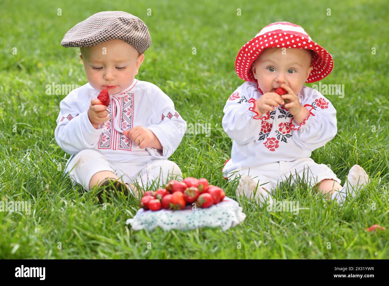 Little boy and girl in russian national costumes eating strawberries in ...
