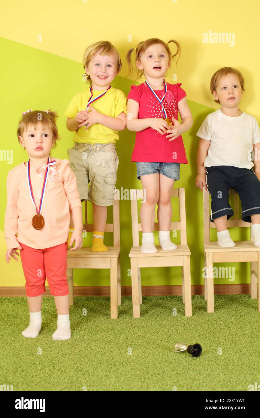 Four children with medals against a bright green wall, three children ...