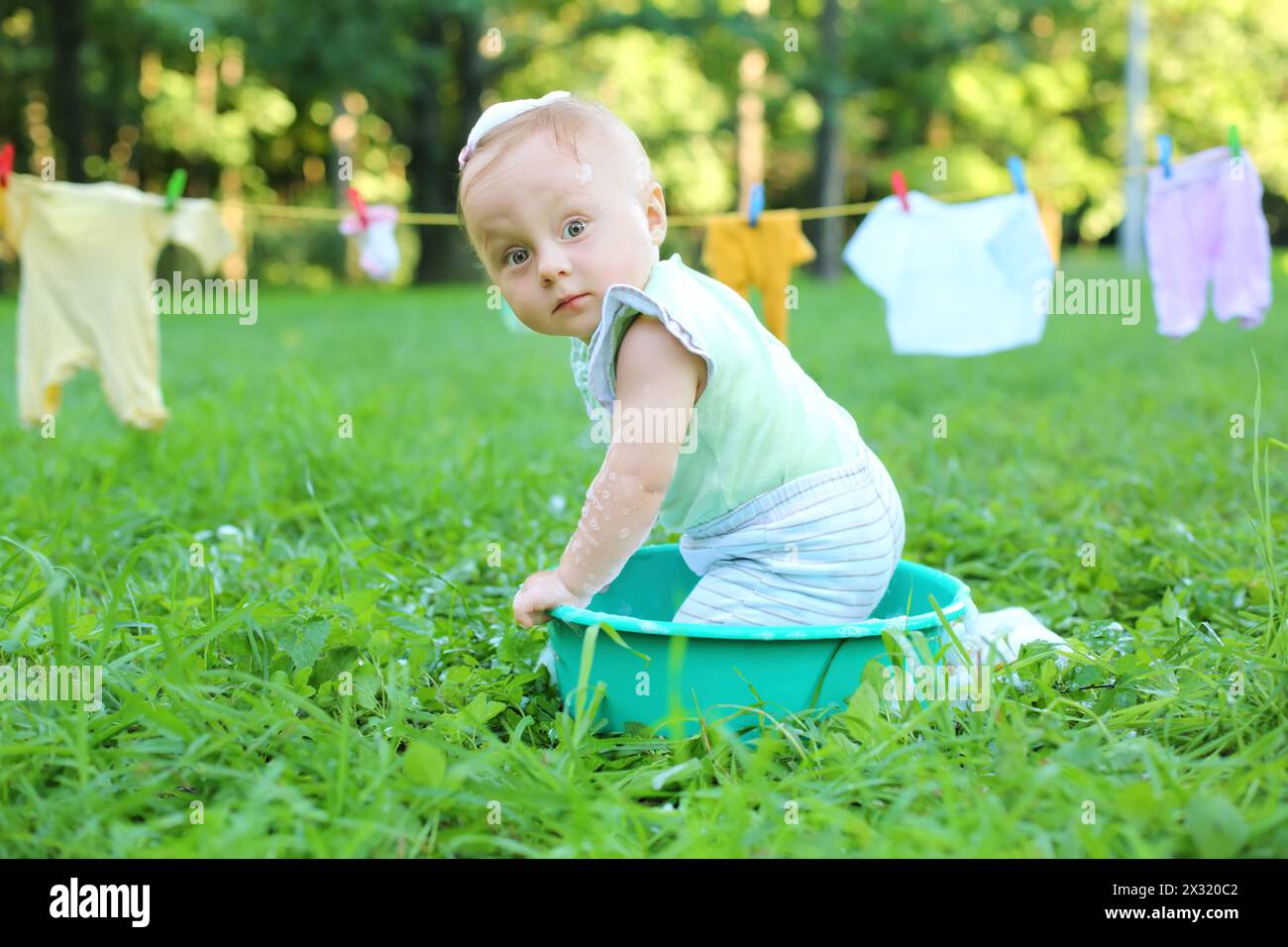 Funny little girl in a small basin with foam near the rope with wash ...