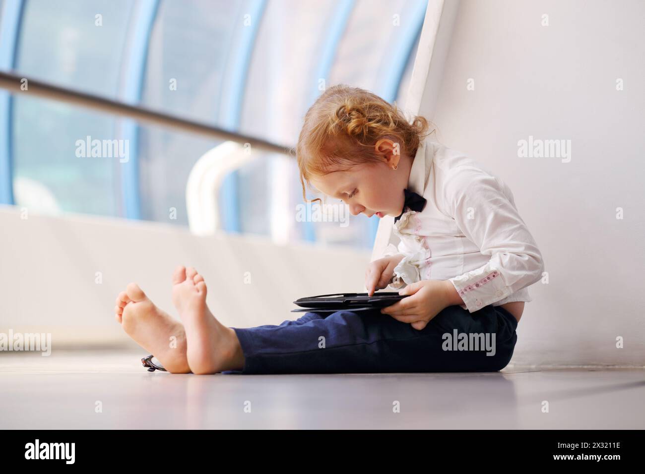 Little cute barefoot girl sits on floor and plays with tablet pc in ...