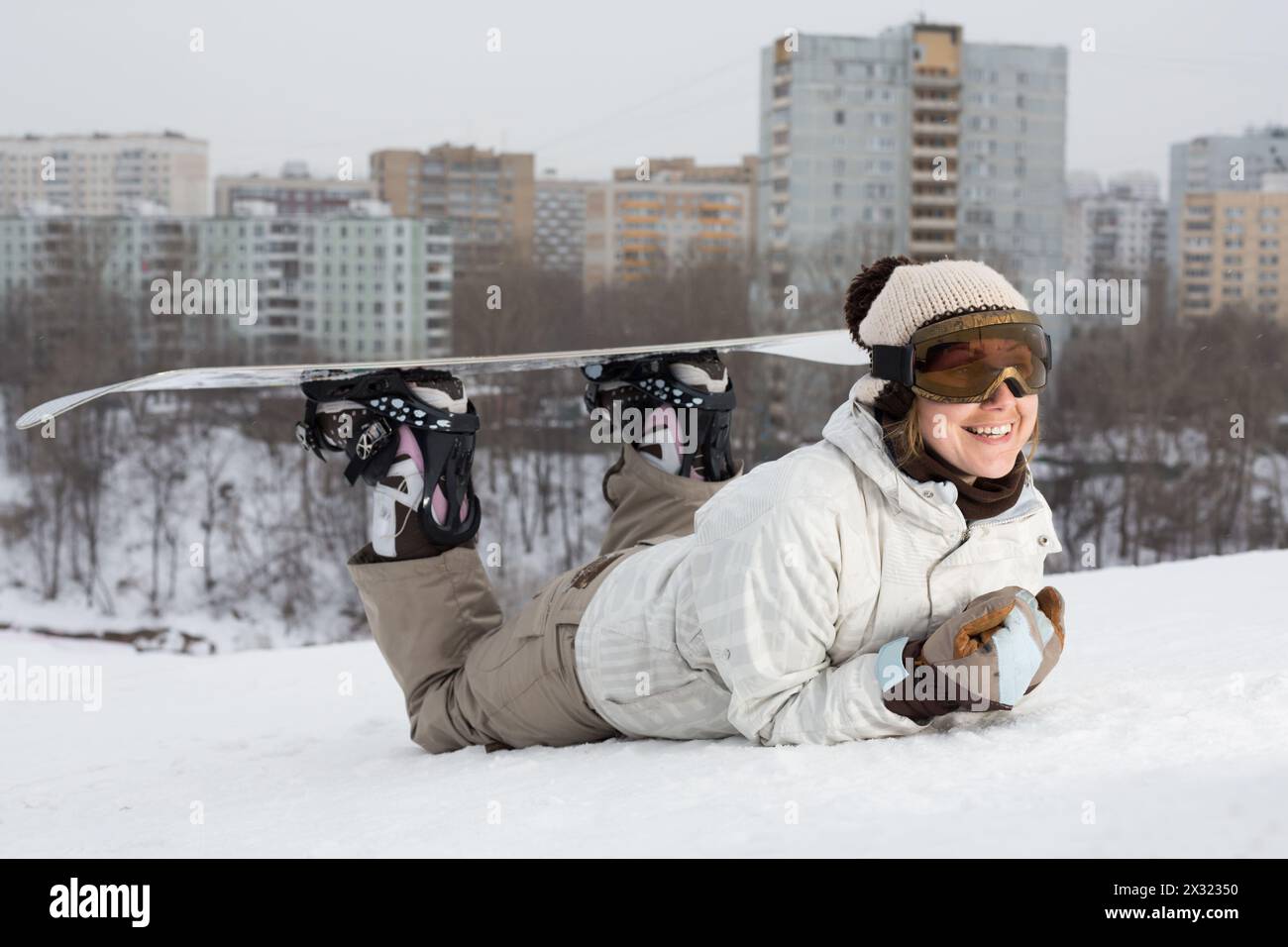 Smiling girl snowboarder in sunglasses lying in the snow on a hill with ...
