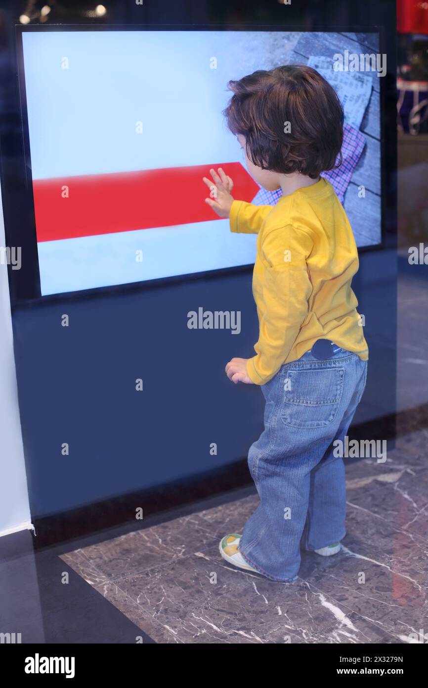 Back of little boy in jeans touching big advertising display at mall ...