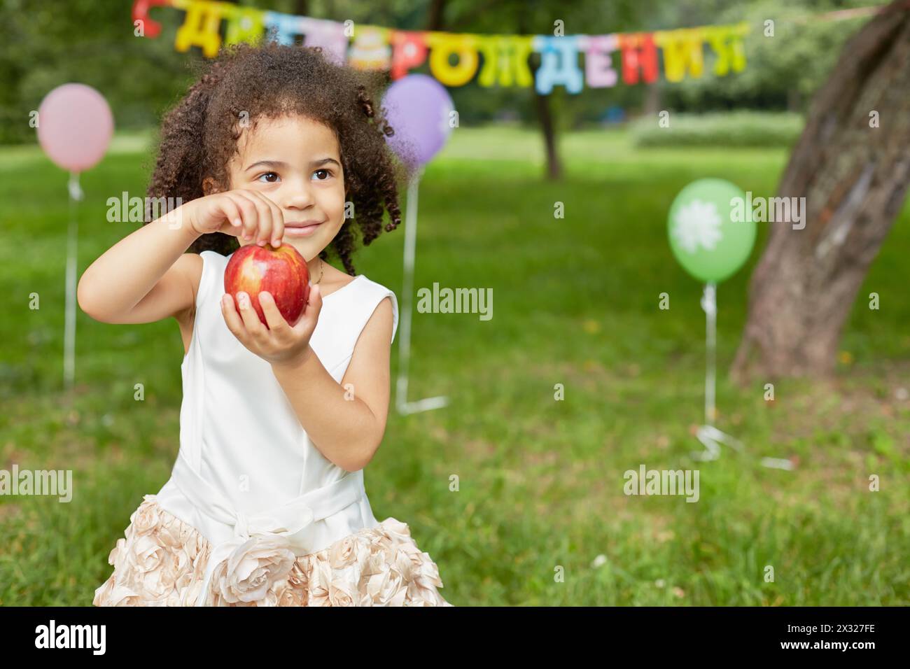 Little girl stands in park, holding big red apple in her hands, happy ...