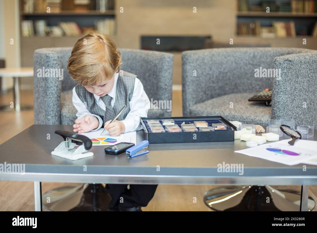 Little cute boy in business clothes draws the diagram on the table ...