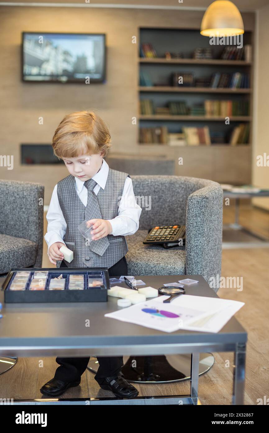 Little boy in business clothes playing with a mineral samples in room ...