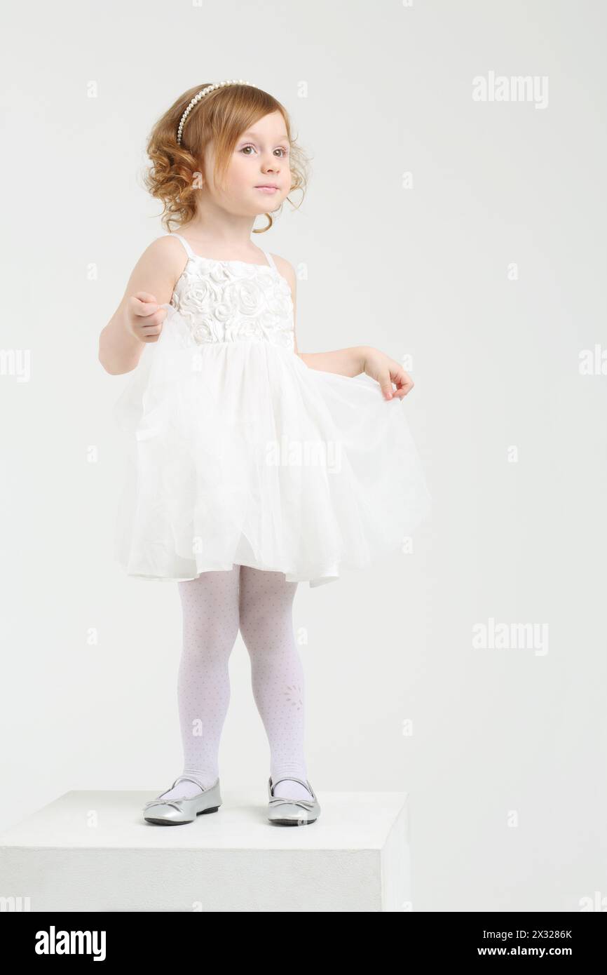 Little girl in white dress poses on big cube on white background Stock ...