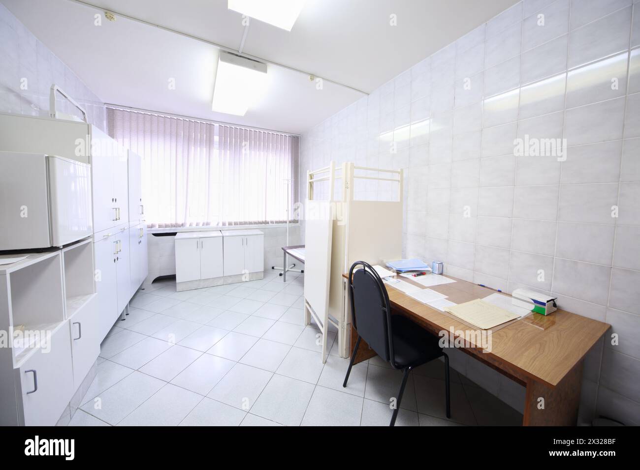 Interior of a light doctors consulting room with table, cabinet and ...