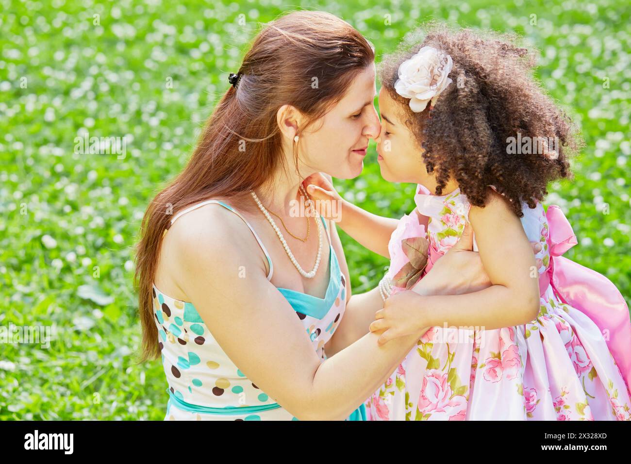 Mother and little daughter rub noses on sunny grassy lawn Stock Photo ...