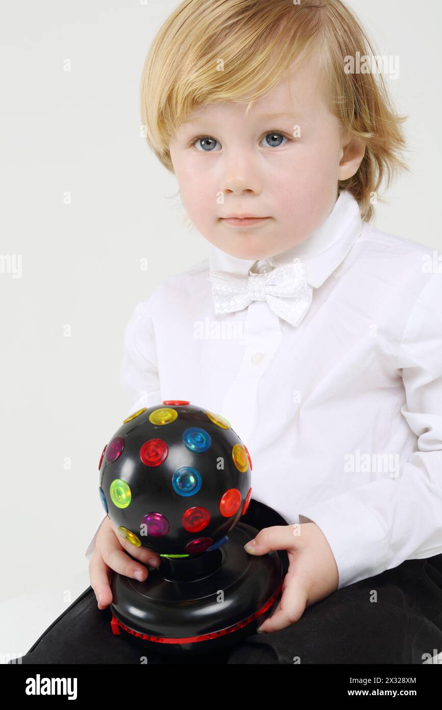 Cute little boy holds ball-shaped lamp and looks away on white ...