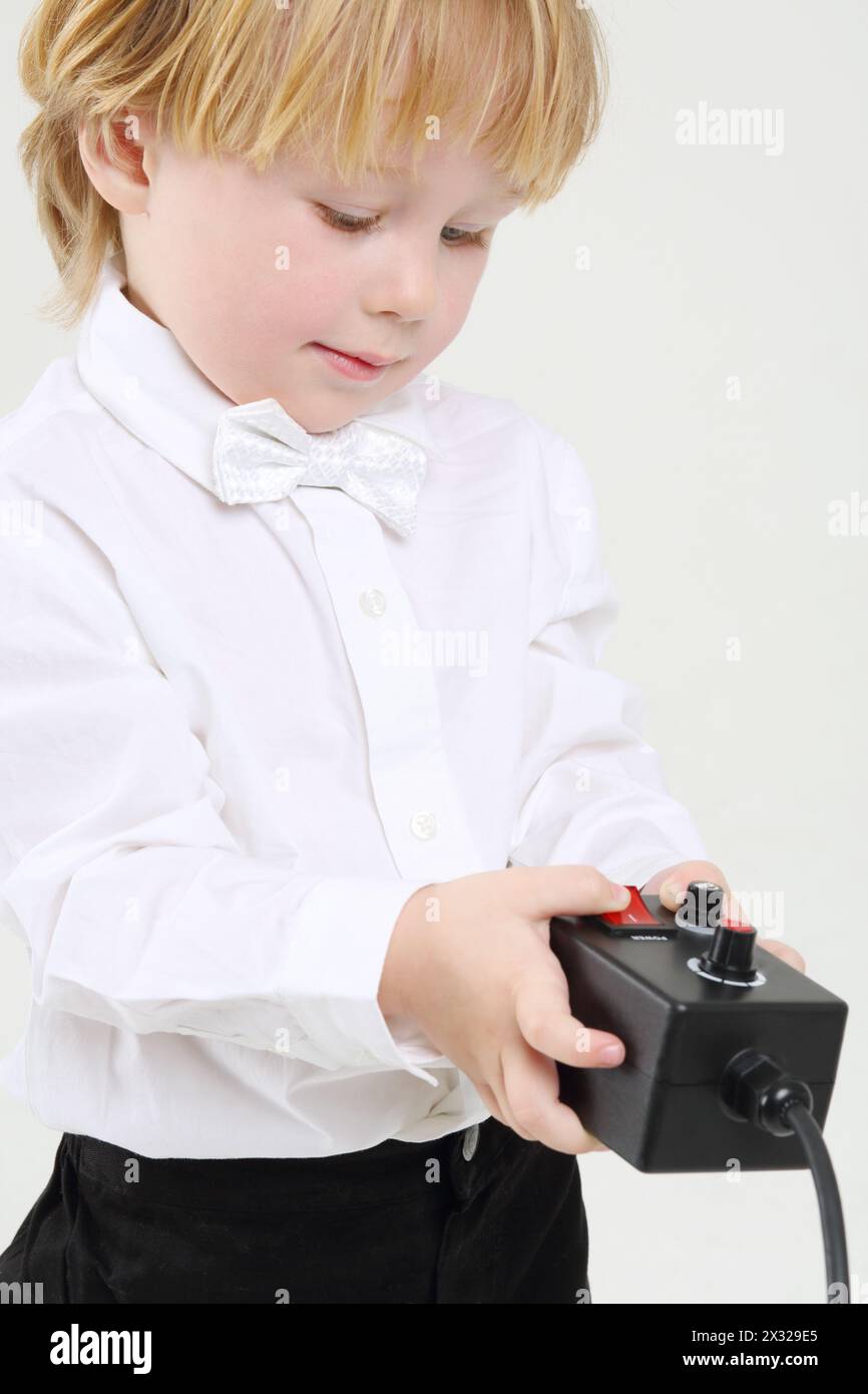 Little blond boy presses button on control console on grey background ...