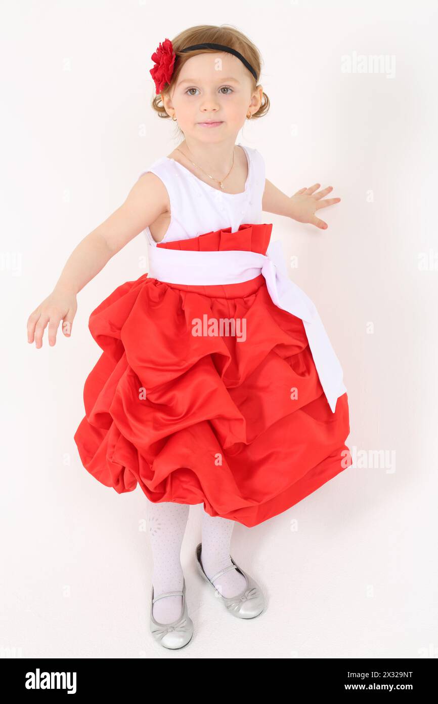 Little girl in beautiful red and white dress poses on grey background ...