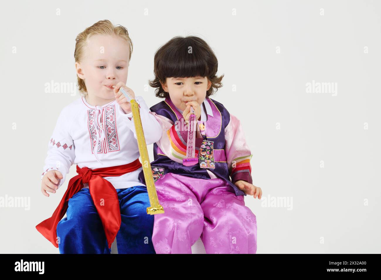 Two happy little boys in national costumes sit and blow in party ...