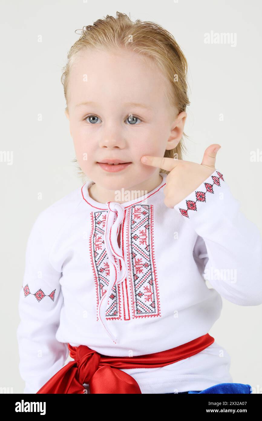 Happy little boy in russian national costume sits and touches cheek by ...