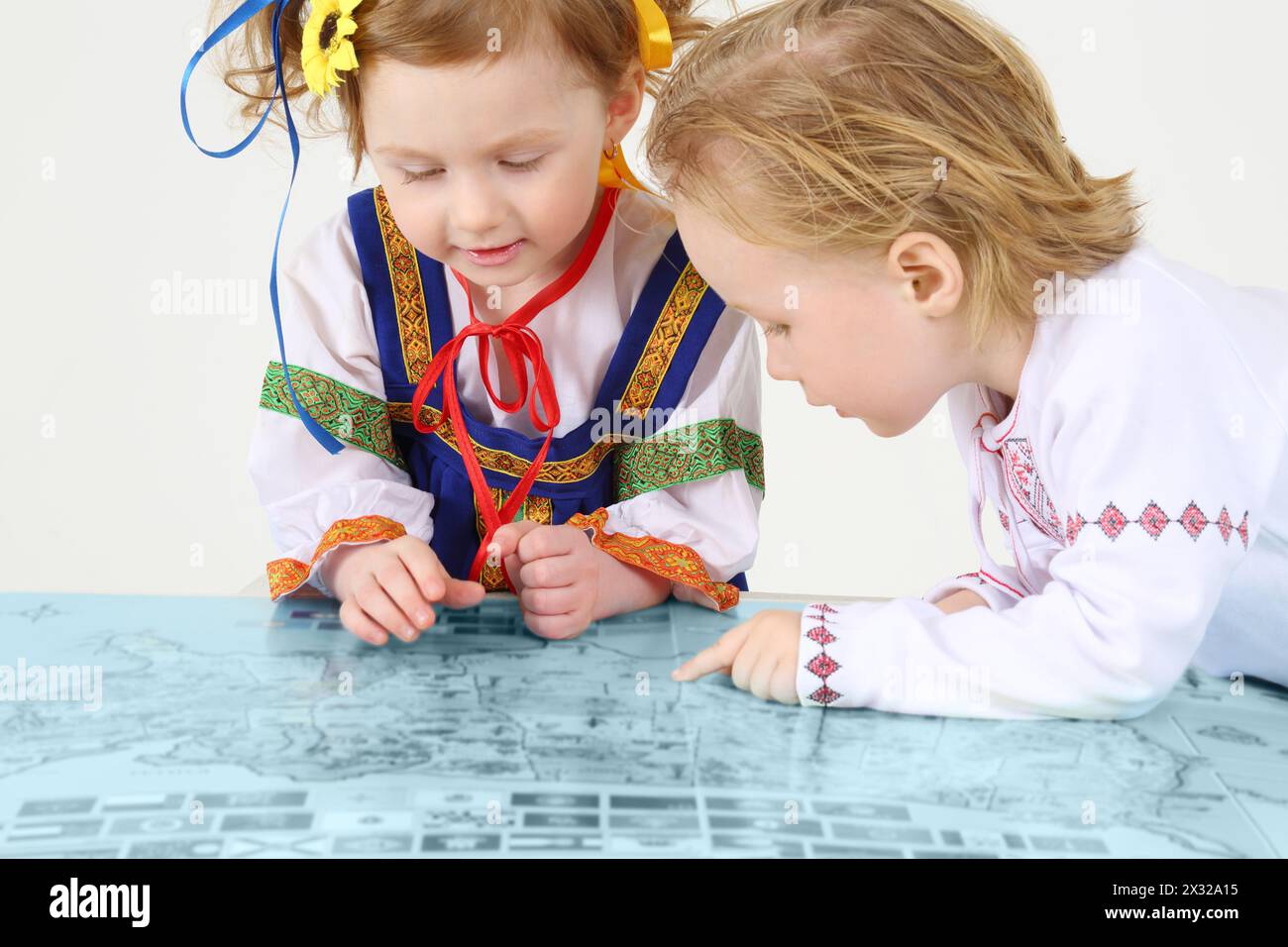 Little boy and girl in Russian folk costumes look at varicolored map on ...