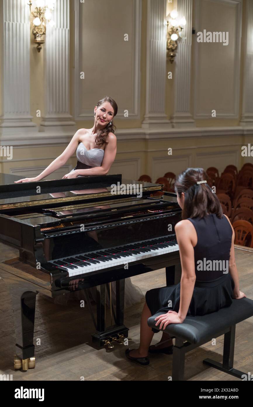 Woman pianist sits at the piano and beautiful singer stands next in ...
