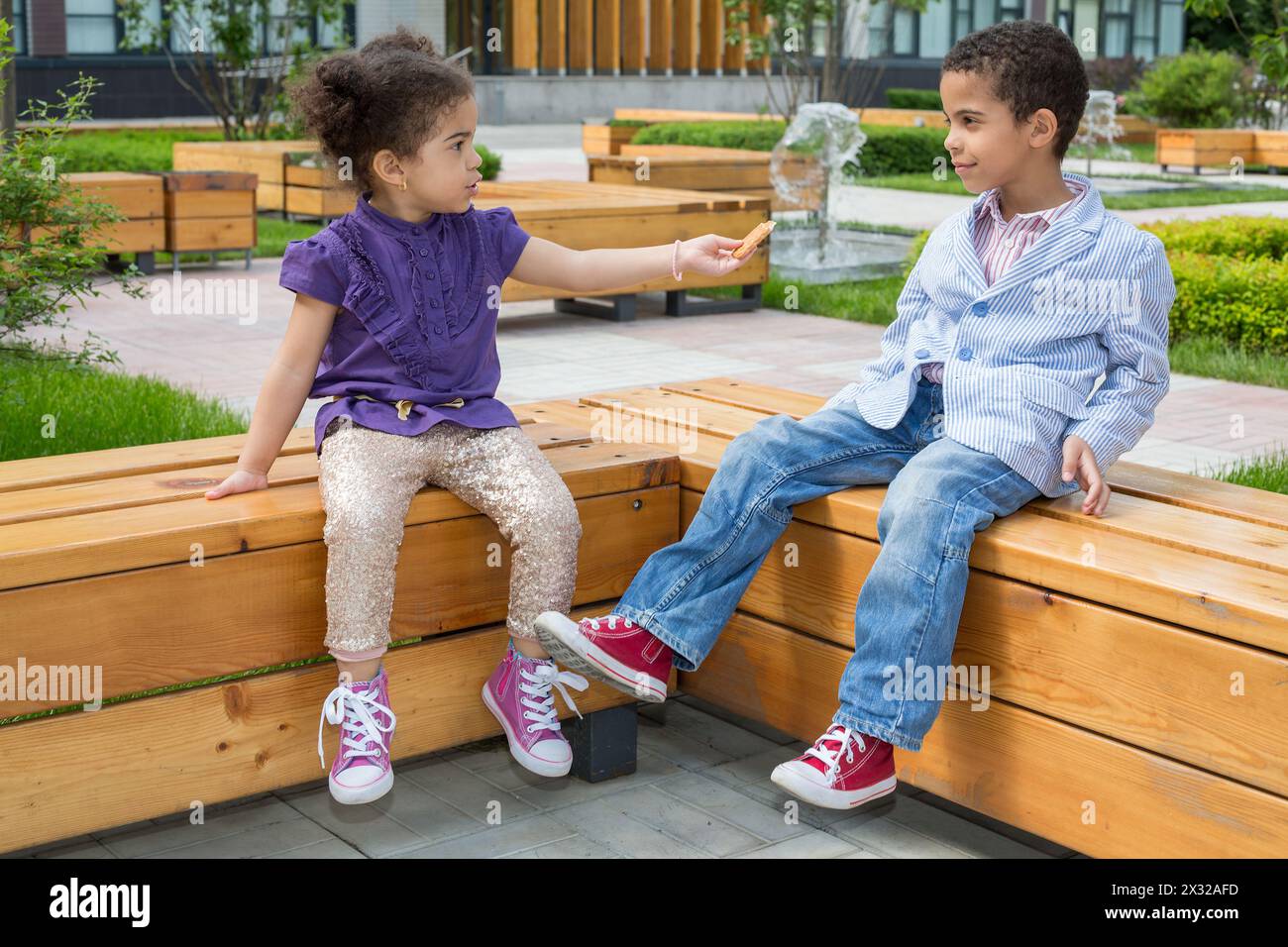 Little girl treats the boy cookies on bench in the park Stock Photo - Alamy