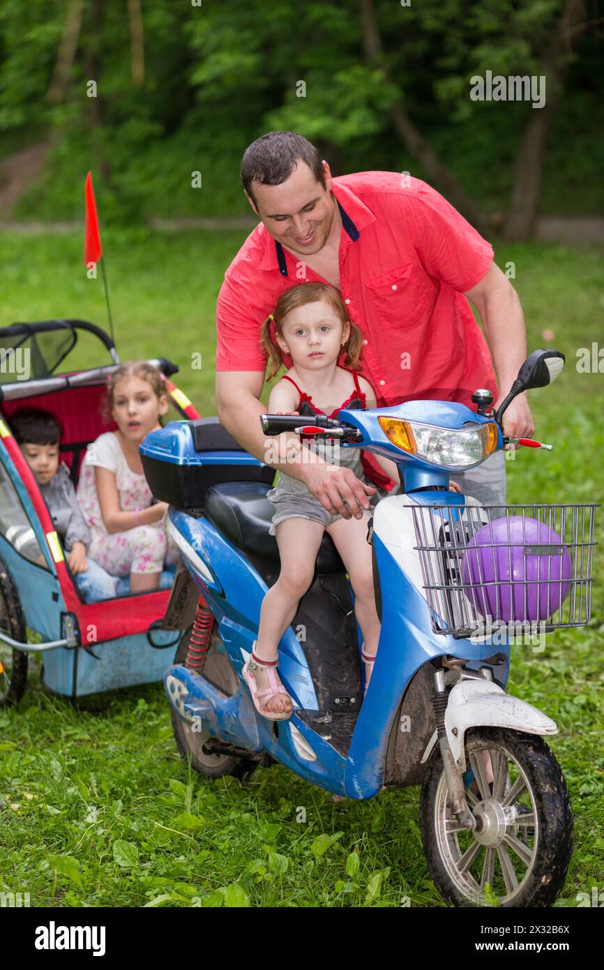 Two children in cart and girl on a scooter with father on nature Stock ...