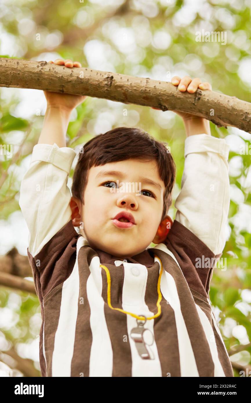 Closeup portrait of little boy who hang on branch grasping at it with ...