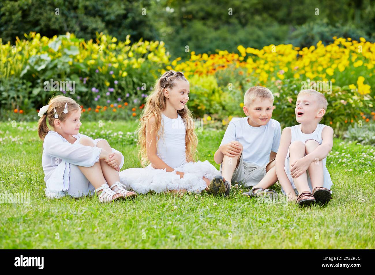 Four children sit on grass at loawn, one boy sings with eyes closed ...