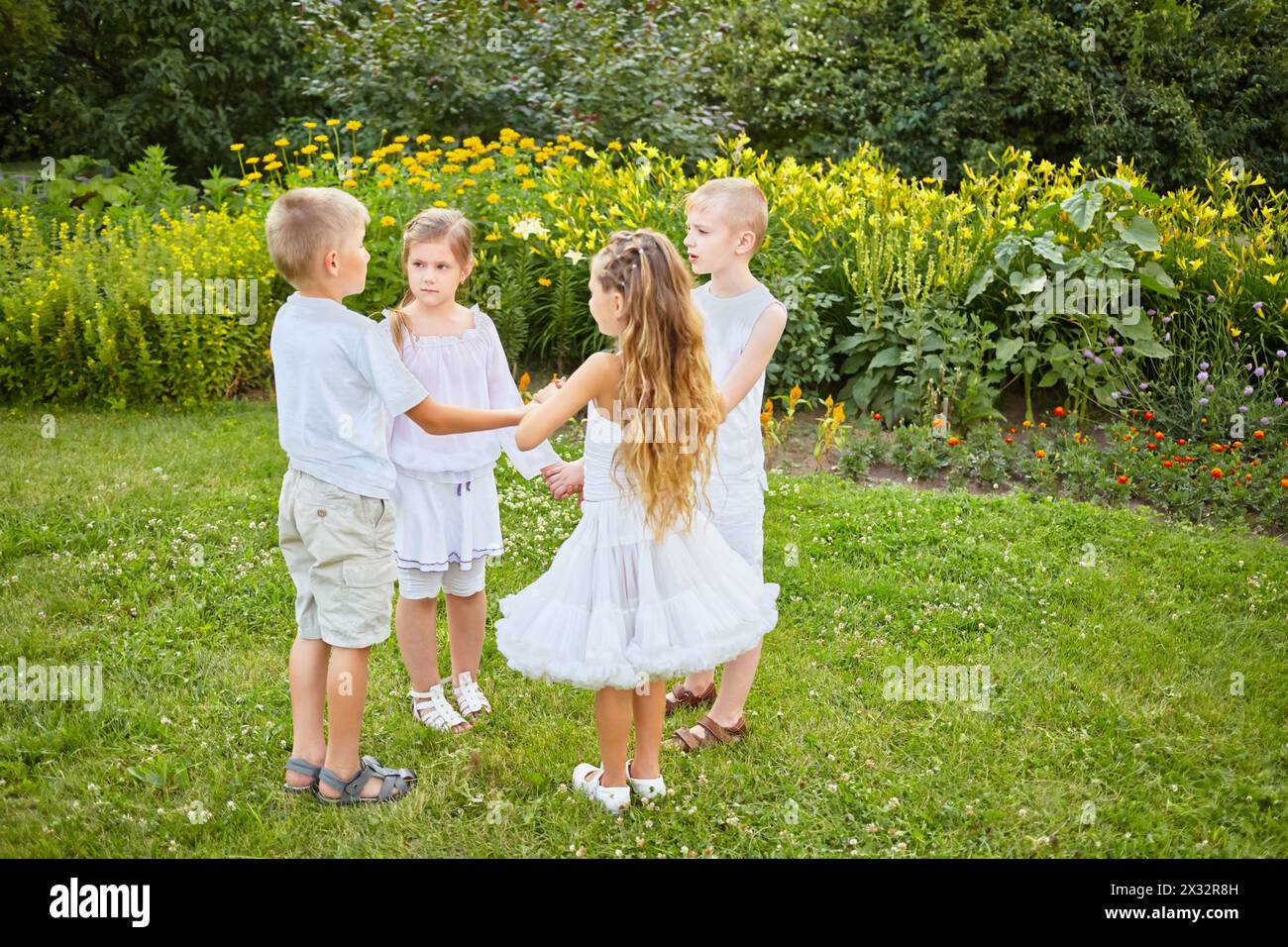 Four children stand in circle holding hands on grassy lawn in summer ...