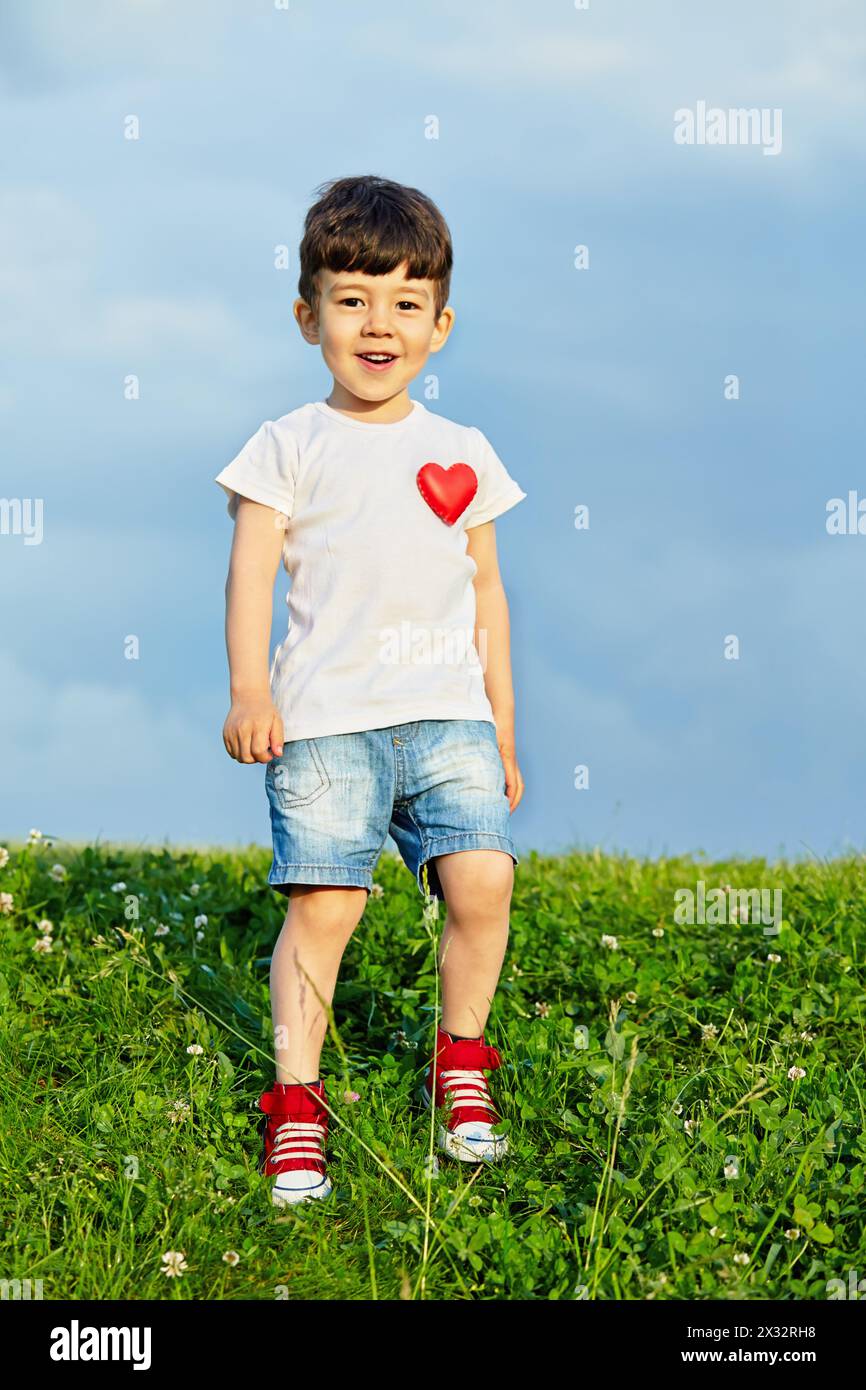 Little boy in shorts and white t-shirt with pinned red heart goes down ...
