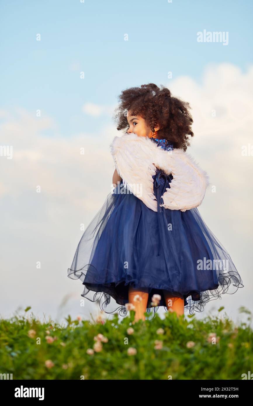Little girl in dark-blue gown with angel wings on her back stands ...