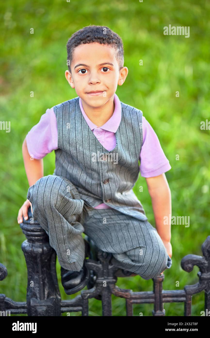Little boy dressed in suit with vest sits on black wrought-iron fence ...